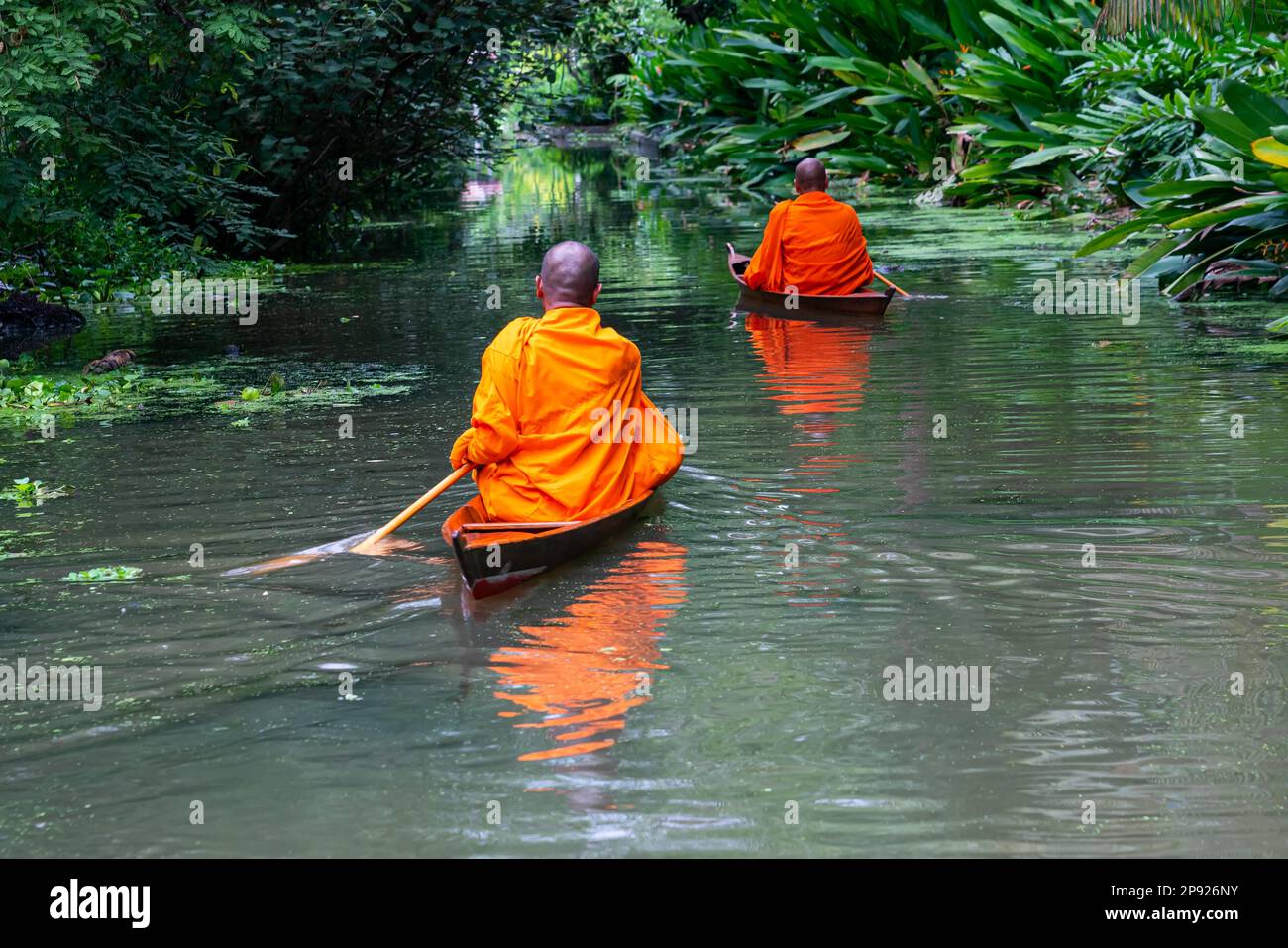 Buddhist monks paddle boat in the canal. Two monks row the small wooden ...