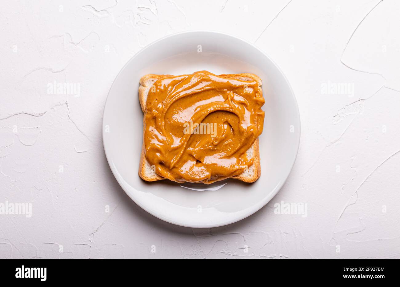Toast with peanut butter on white ceramic plate, white concrete ...