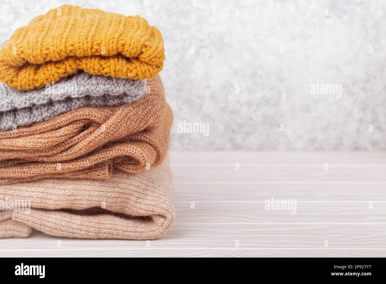 Pile of warm knitted clothes, sweaters and caps on rustic white wooden ...