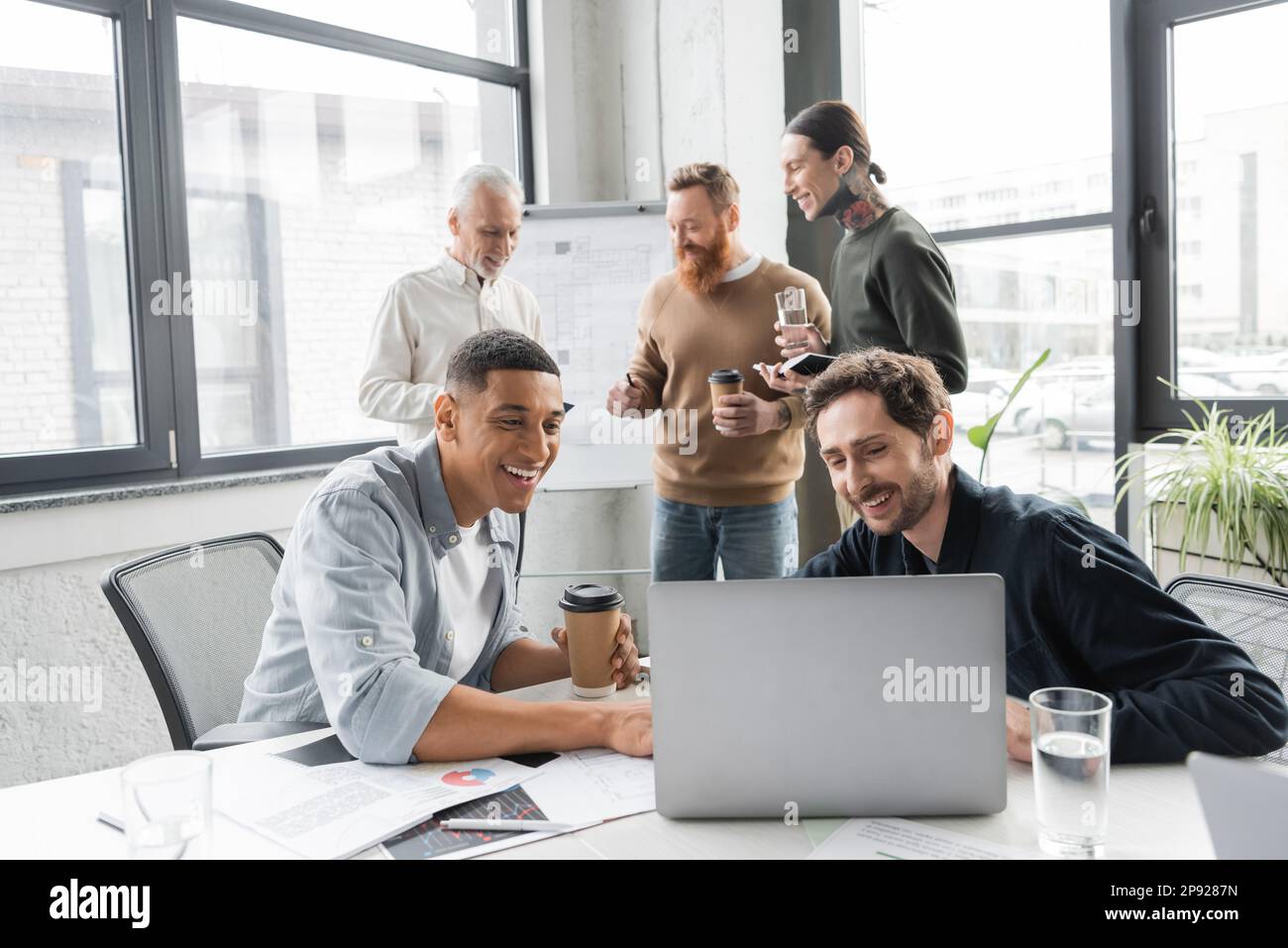 Positive multiethnic businessmen using laptop near colleagues during ...