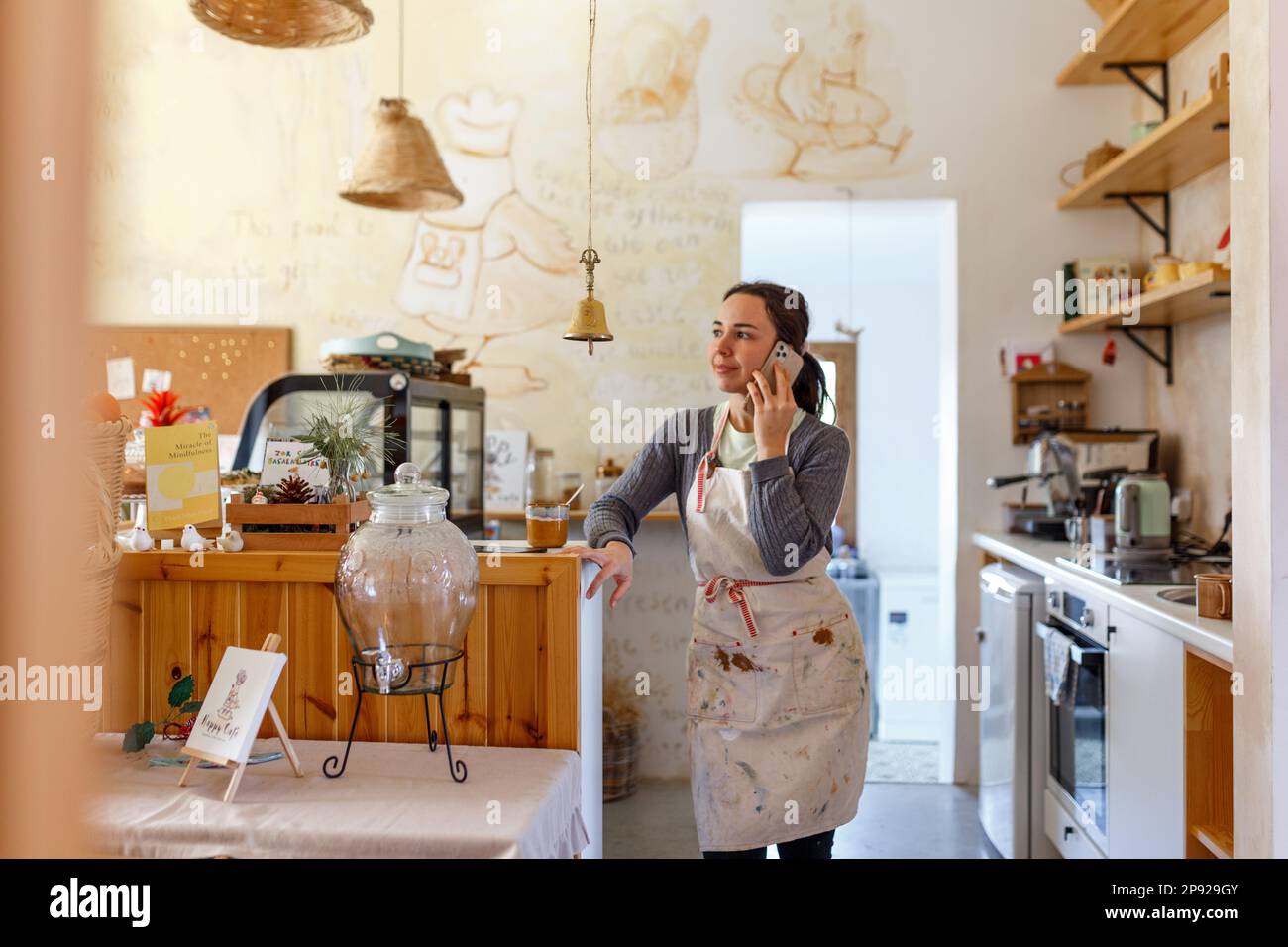 Young female barista standing behind the bar in cafe talking on ...
