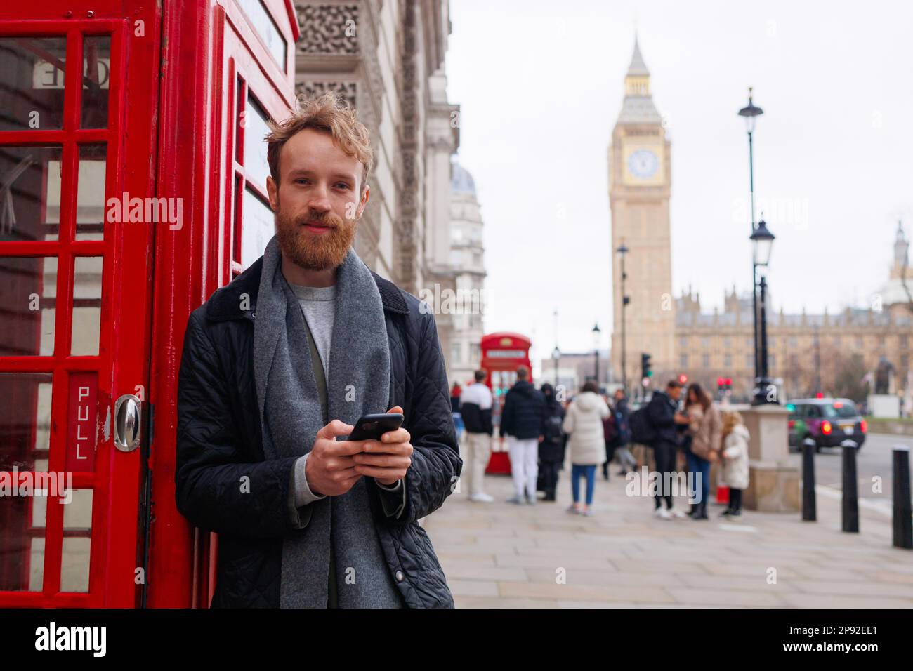 Man with a smartphone in his hands standing near a red telephone booth ...