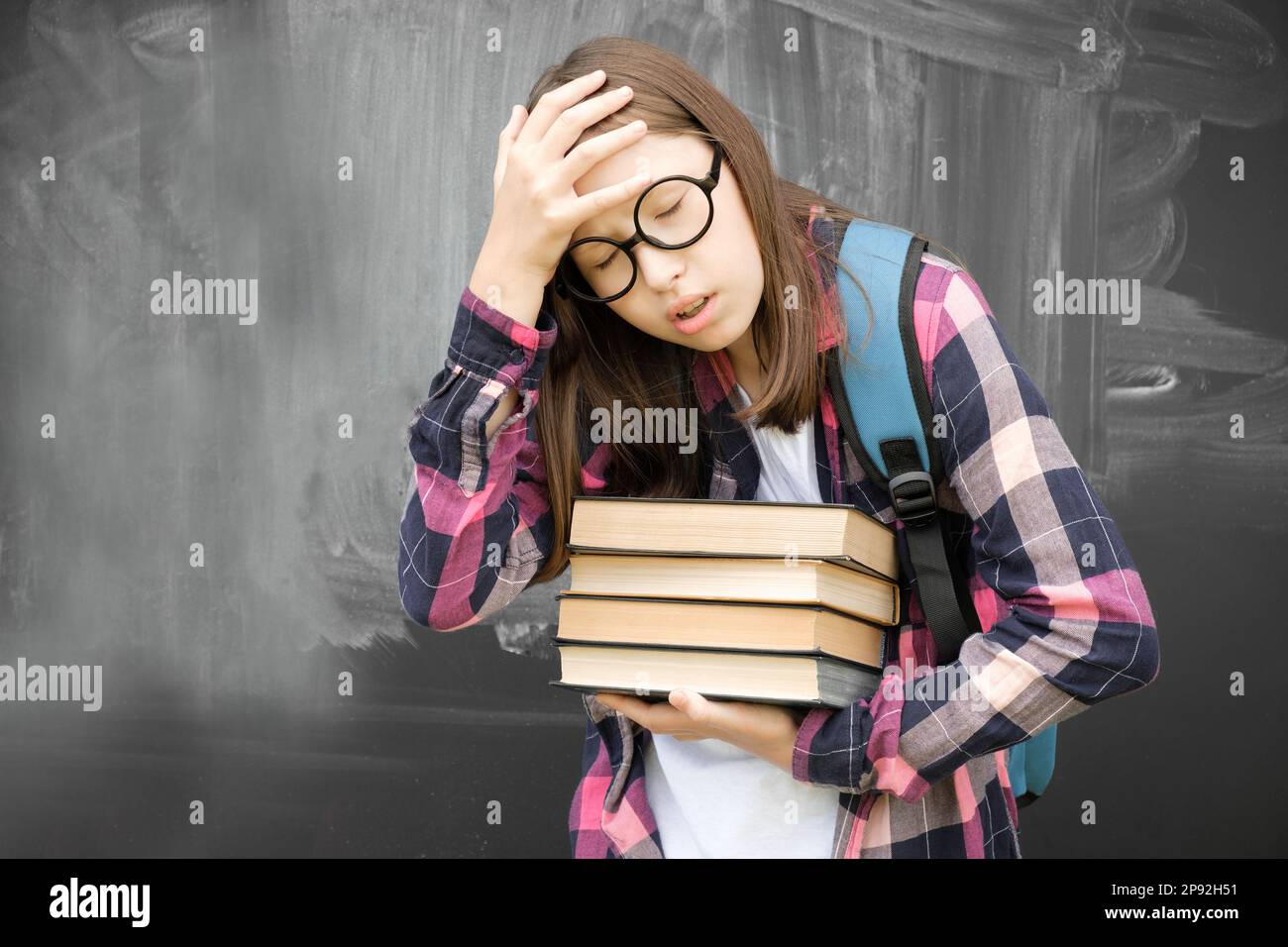 Teen girl little student holding pile of heavy books on chalkboard ...