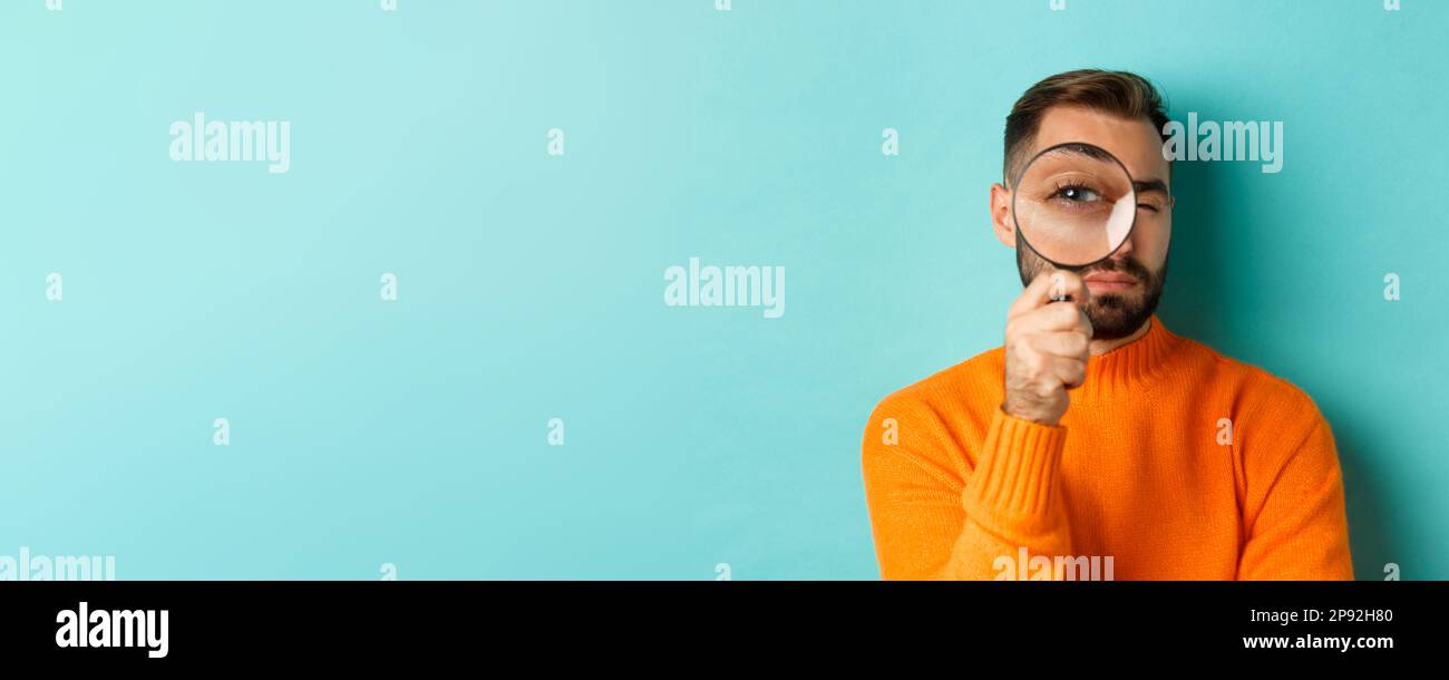 Funny man looking through magnifying glass, searching or investigating ...