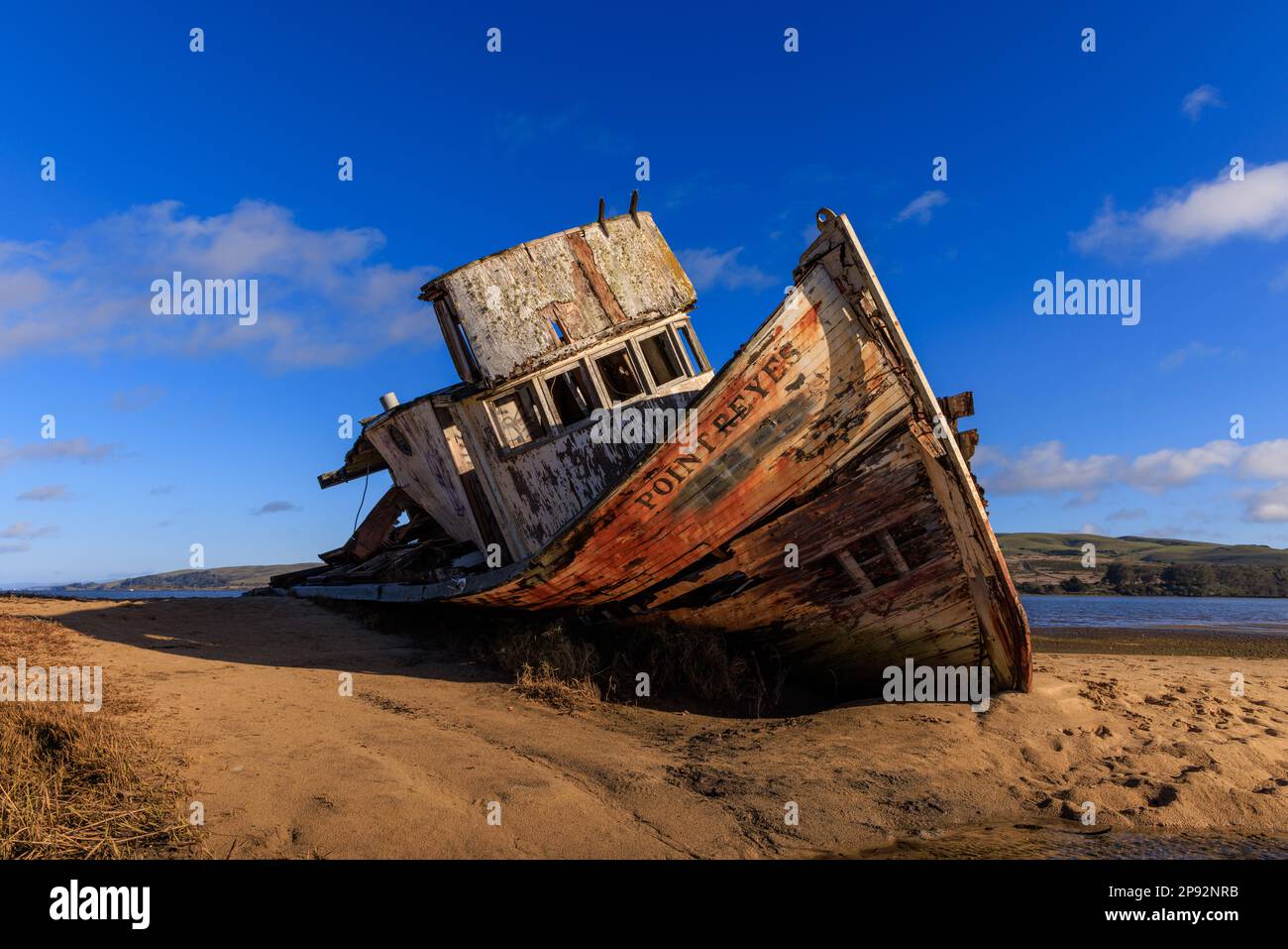 Historic wooden fishing boat wreck on sandy beach in sun and blue sky ...