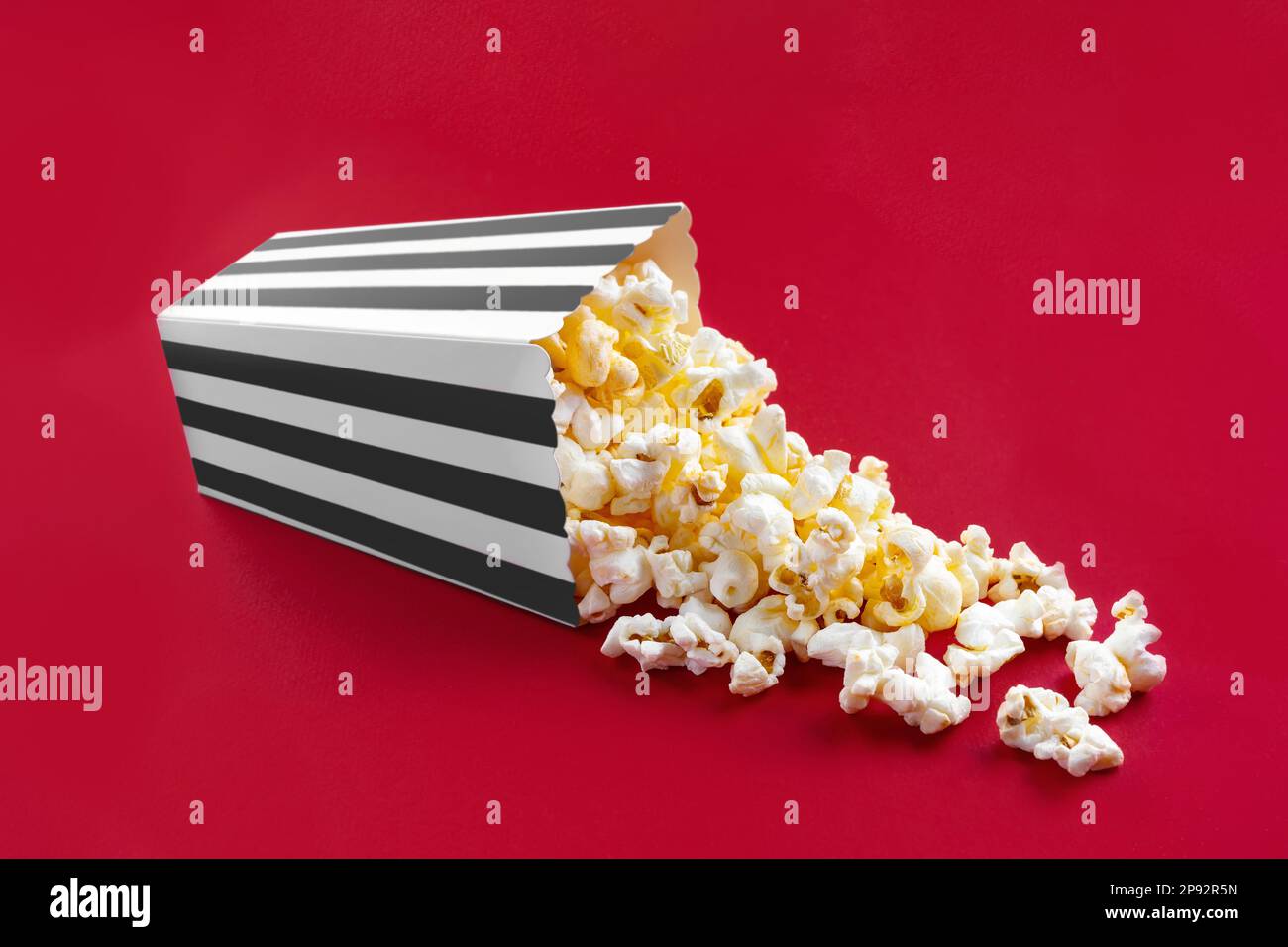 Tasty cheese popcorn falling out of a black striped carton bucket ...