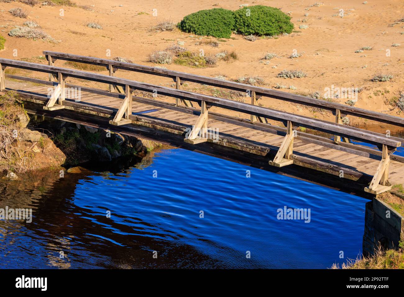 Wooden footbridge over blue water in dry desert sand dunes Stock Photo ...