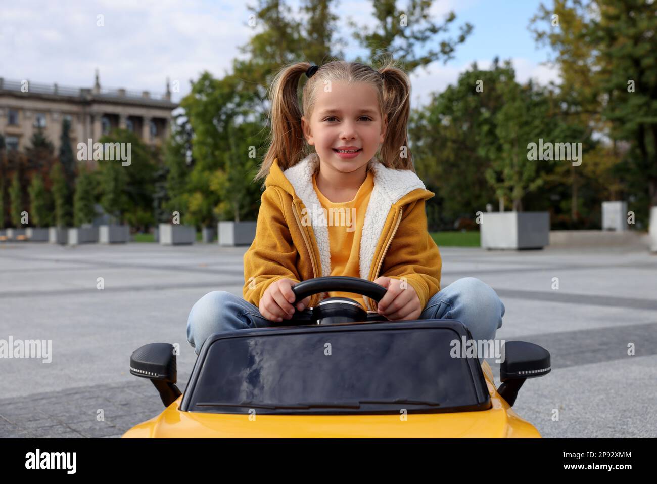 Cute little girl driving children's car on city street Stock Photo - Alamy