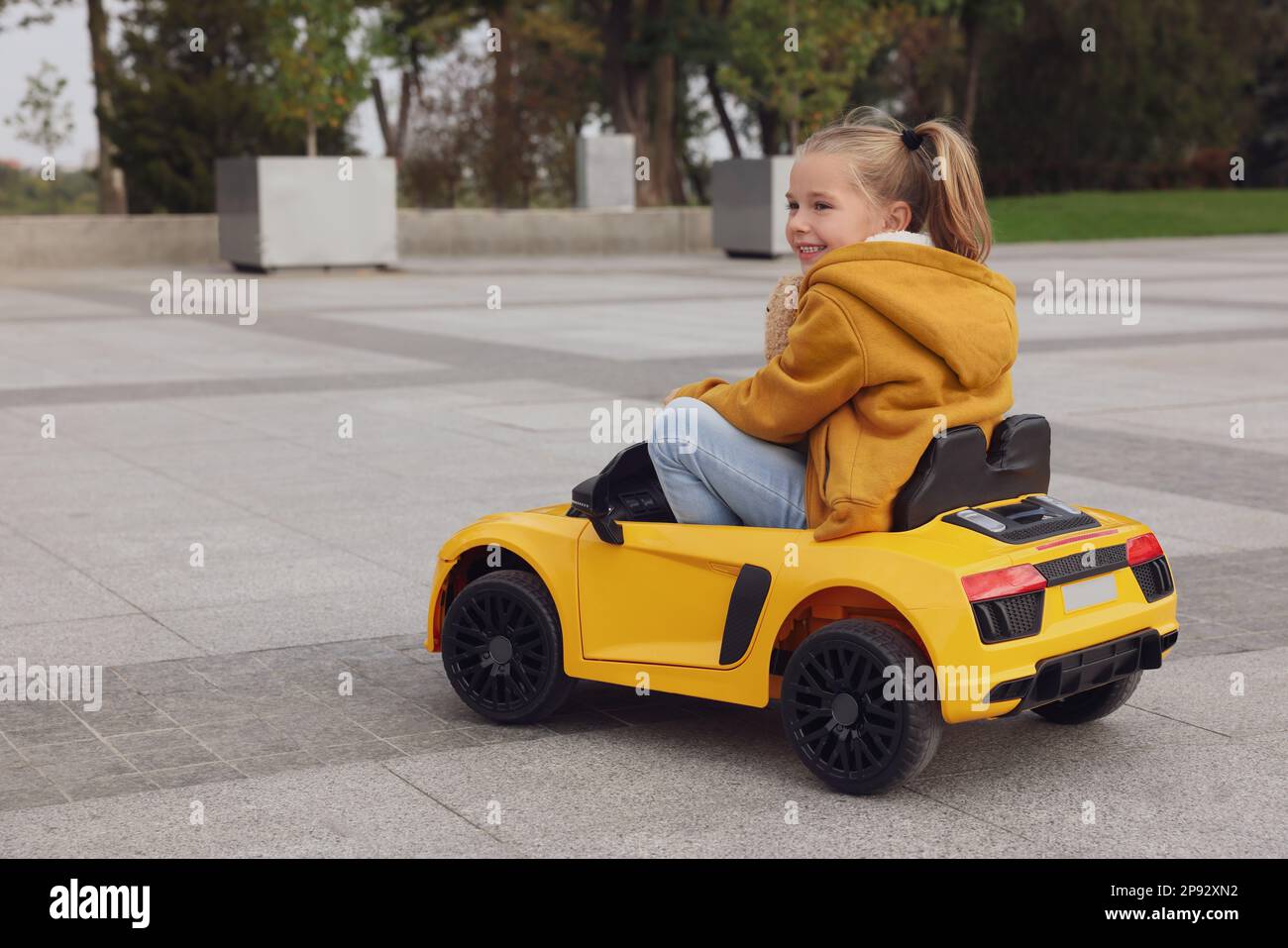 Cute little girl driving children's car on city street. Space for text ...