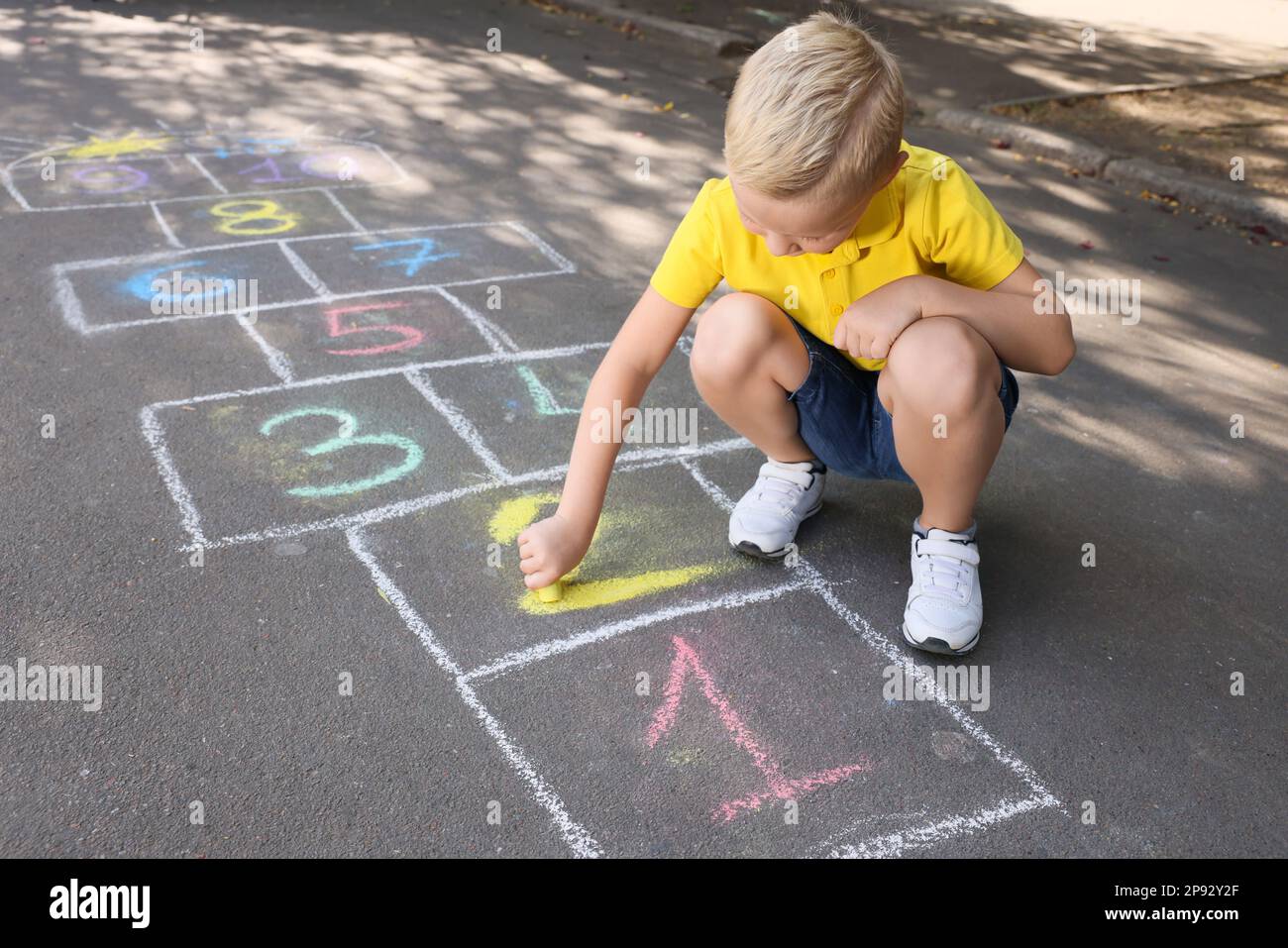 Little boy drawing hopscotch with chalk on asphalt outdoors. Happy ...
