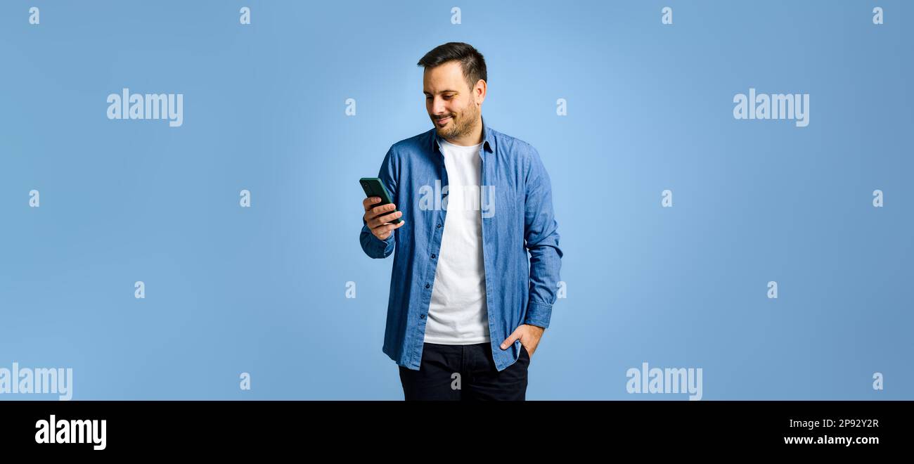 Man with one hand in pocket using smart phone while standing against ...