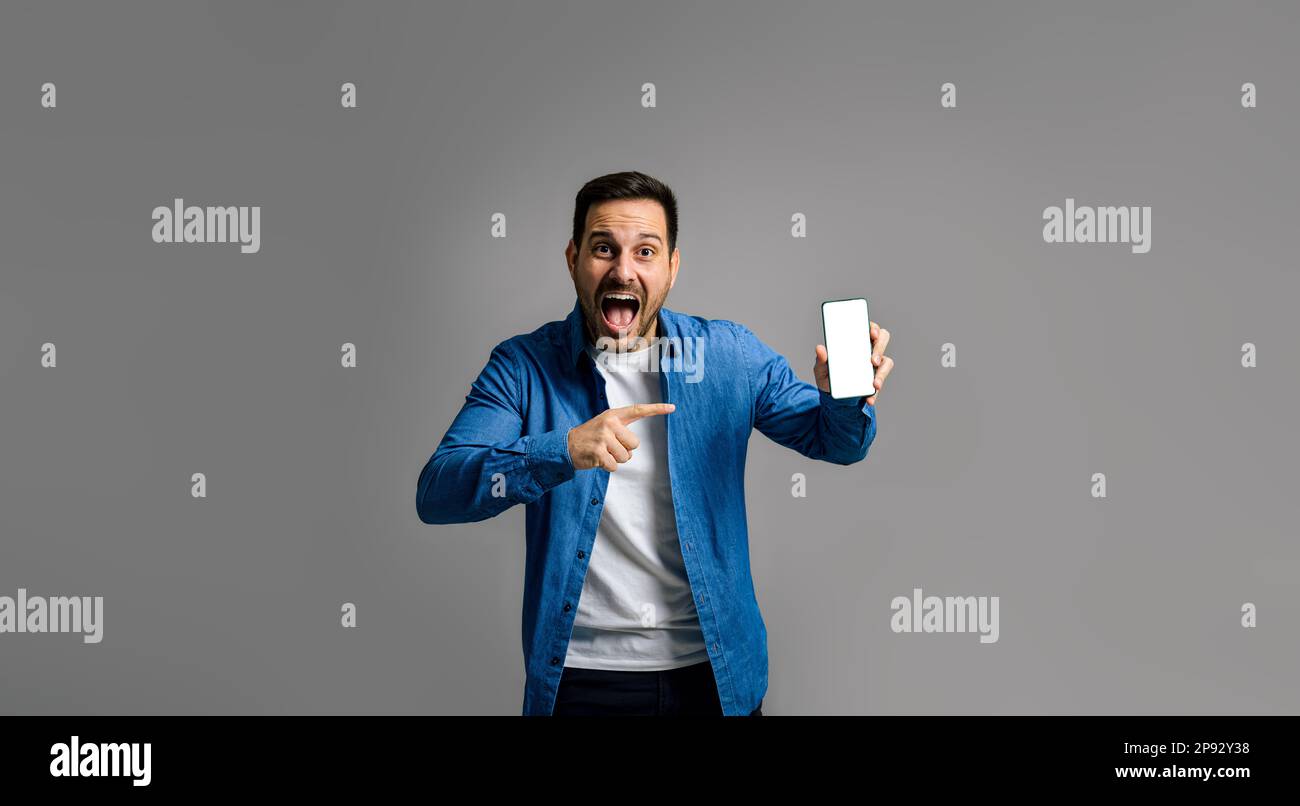 Ecstatic man shouting and pointing at smart phone screen while standing ...