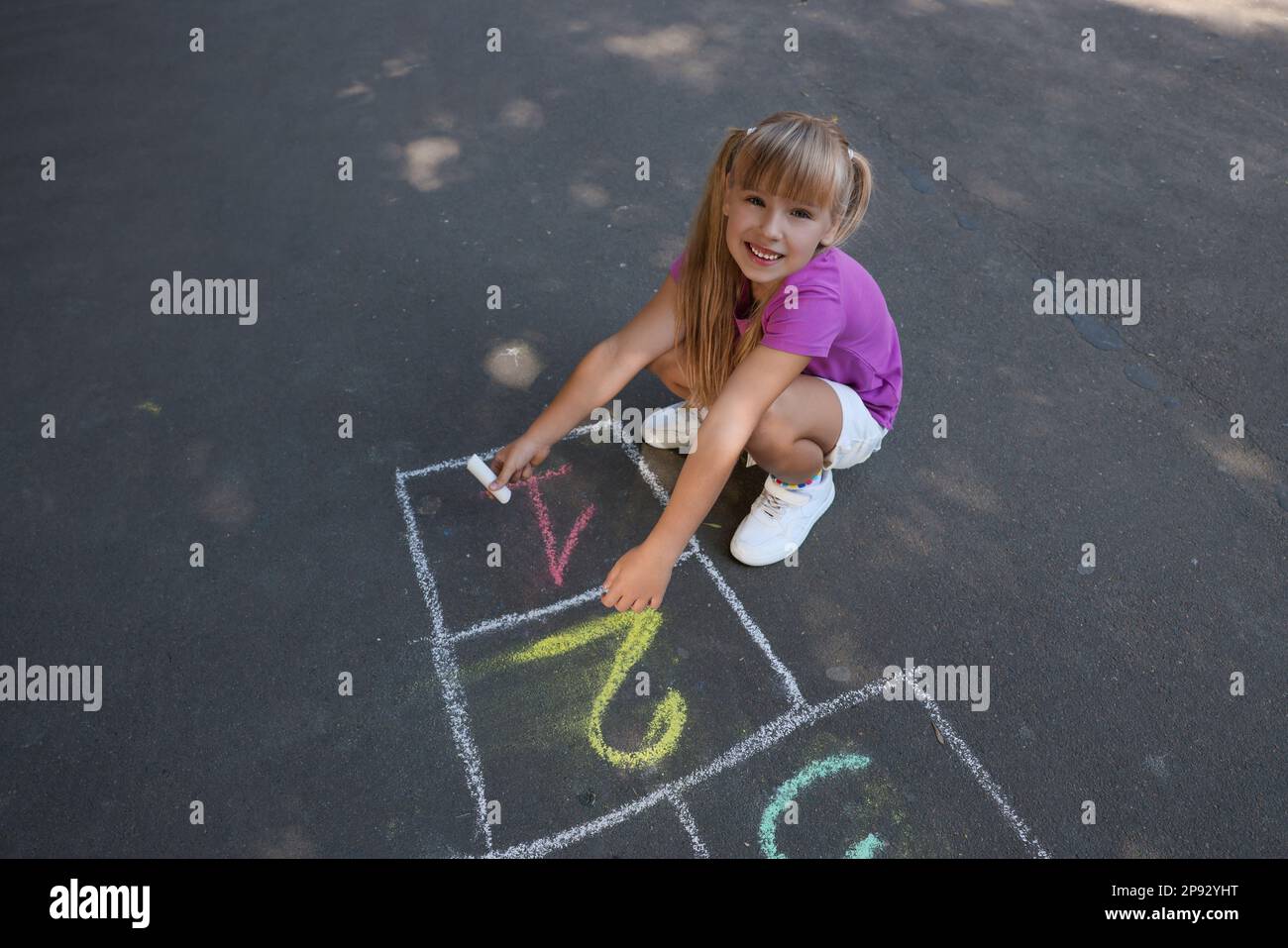 Little girl drawing hopscotch with chalk on asphalt outdoors. Happy ...
