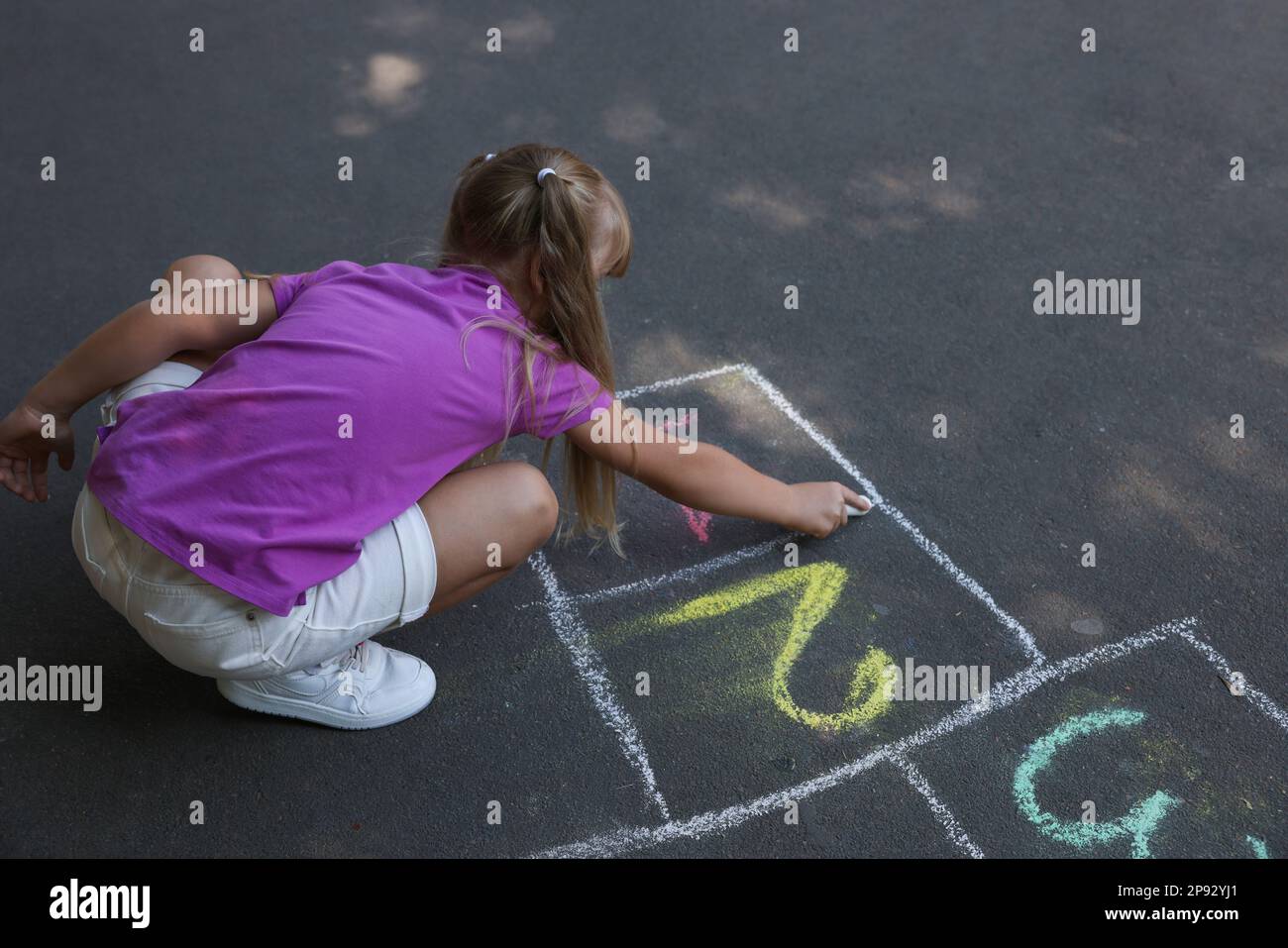 Little girl drawing hopscotch with chalk on asphalt outdoors. Happy ...
