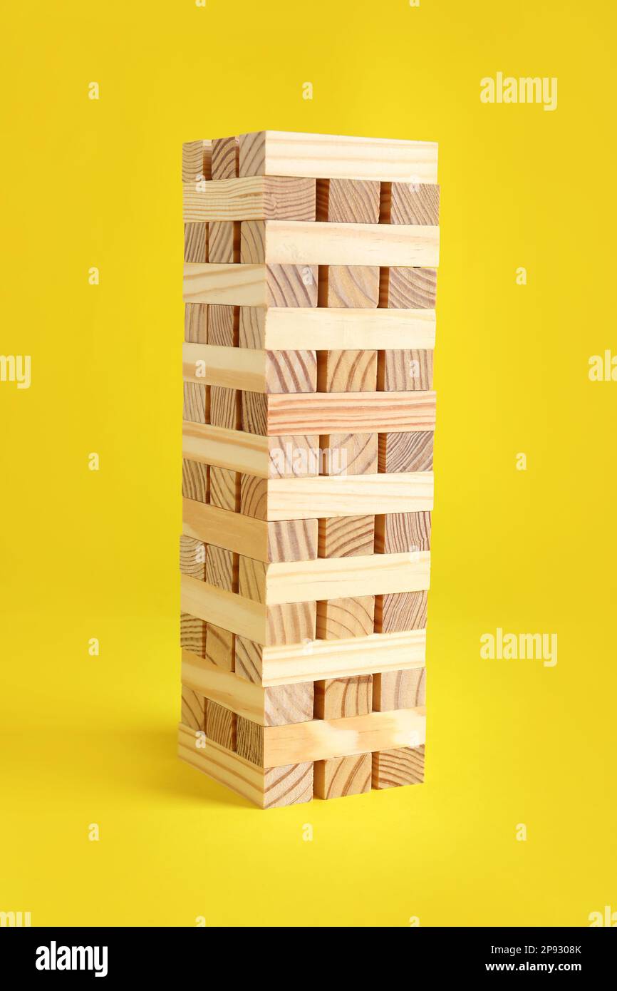 Jenga tower made of wooden blocks on yellow background Stock Photo - Alamy
