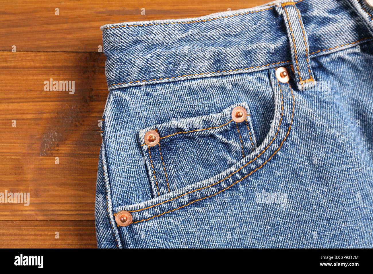 Stylish light blue jeans on wooden background, closeup of inset pocket ...