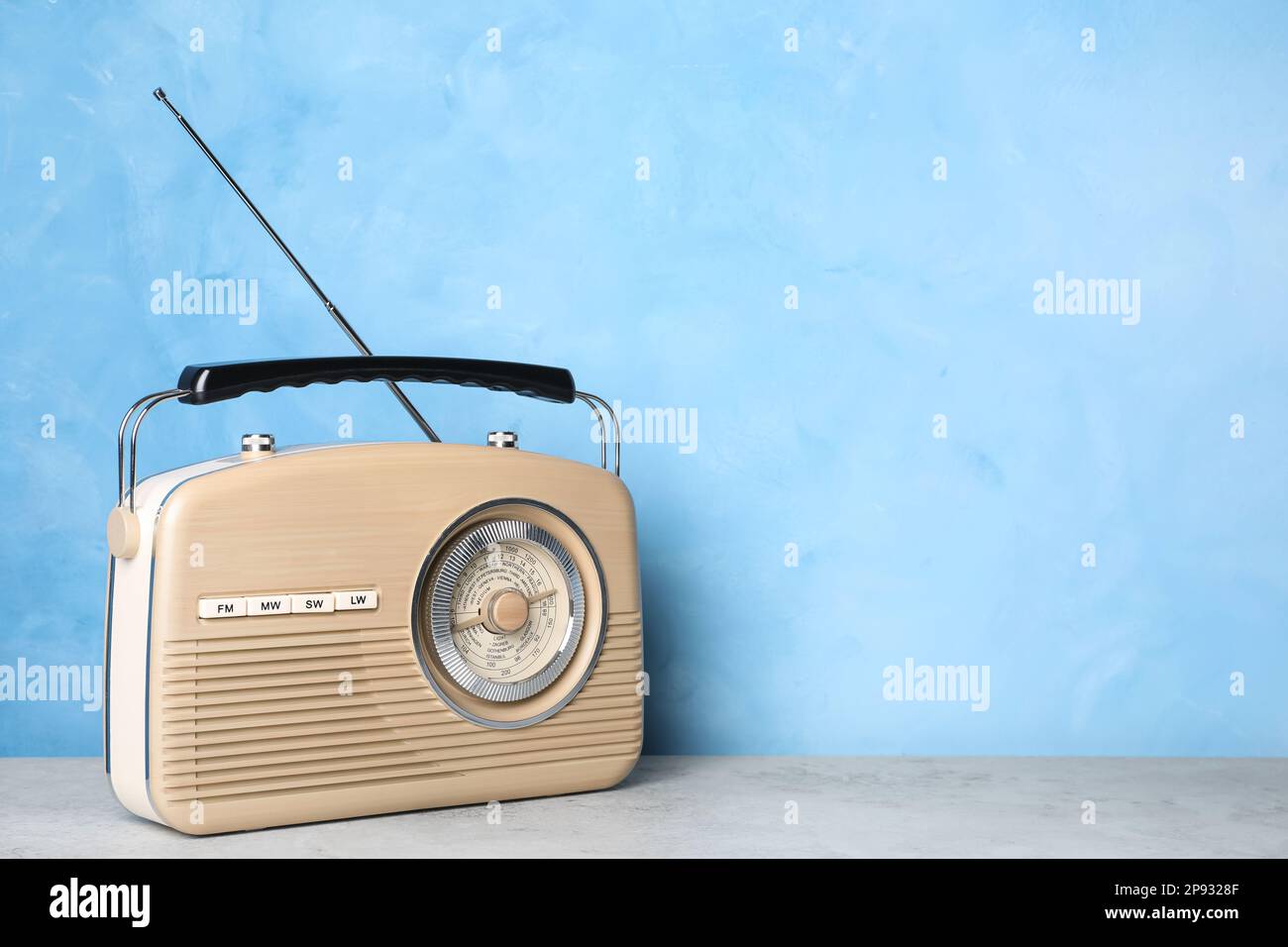 Retro radio receiver on grey table against light blue background. Space ...