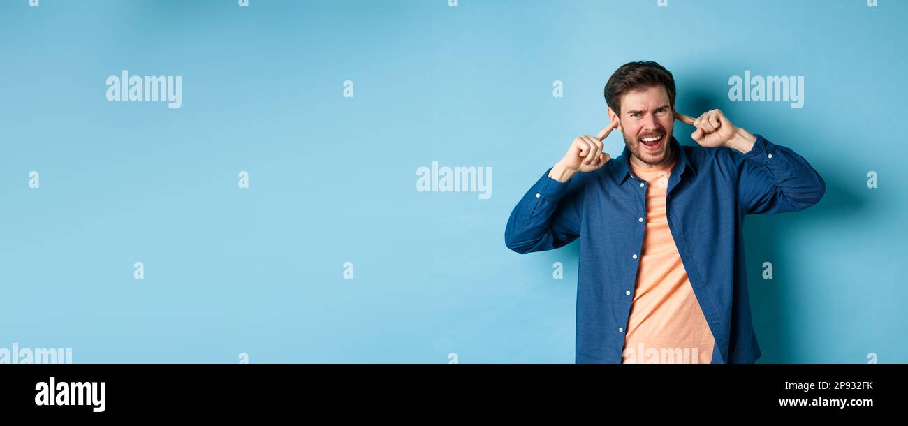 Angry guy shouting with shut ears, block loud music and frowning ...