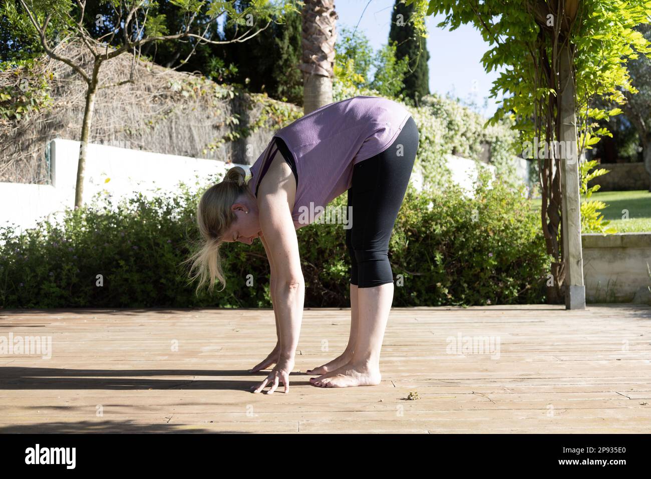 Woman in pre-bend during her yoga practice on a terrace in the sun ...