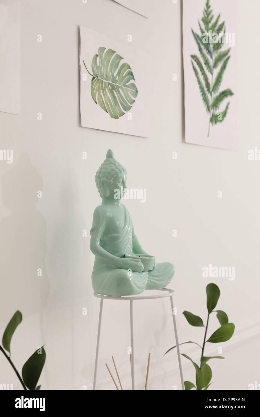 Ceramic Buddha sculpture near wall with floral paintings indoors ...