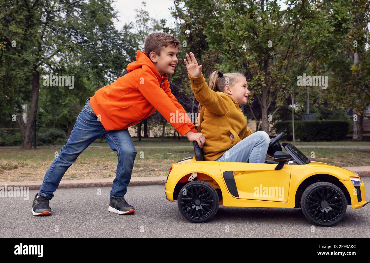 Cute boy pushing children's car with little girl outdoors Stock Photo ...