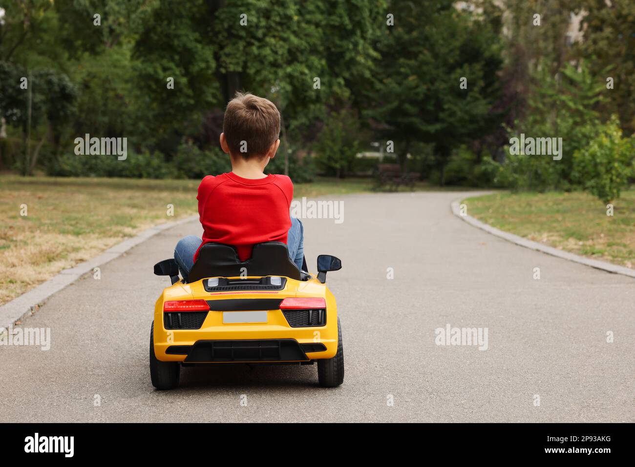 Cute little boy driving children's car outdoors, back view. Space for ...