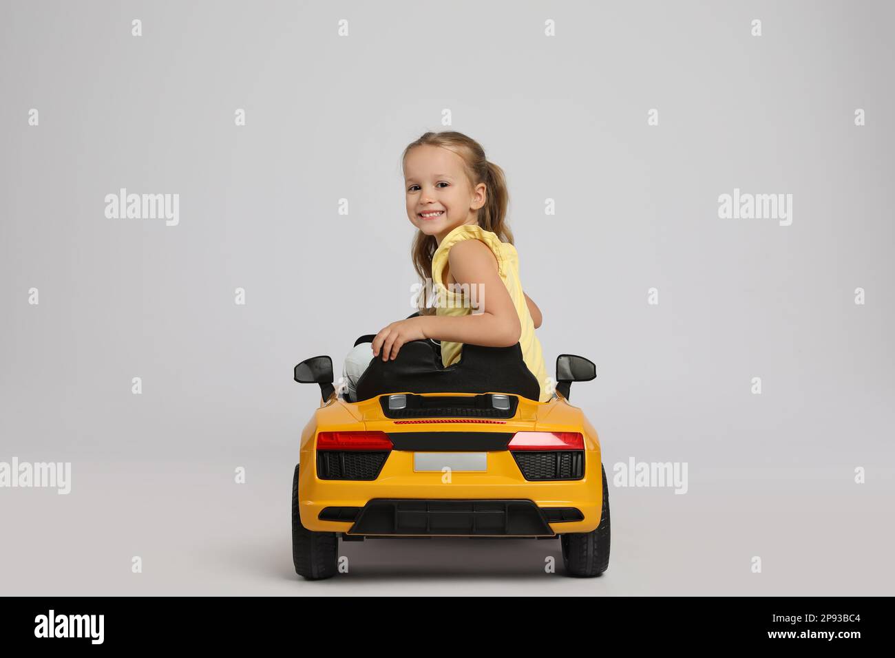 Cute little girl driving children's electric toy car on grey background ...