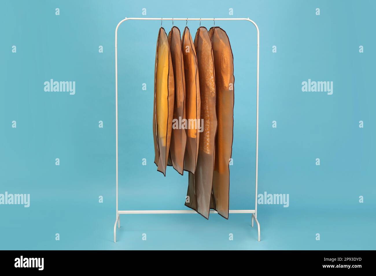 Garment bags with clothes on rack against light blue background Stock ...