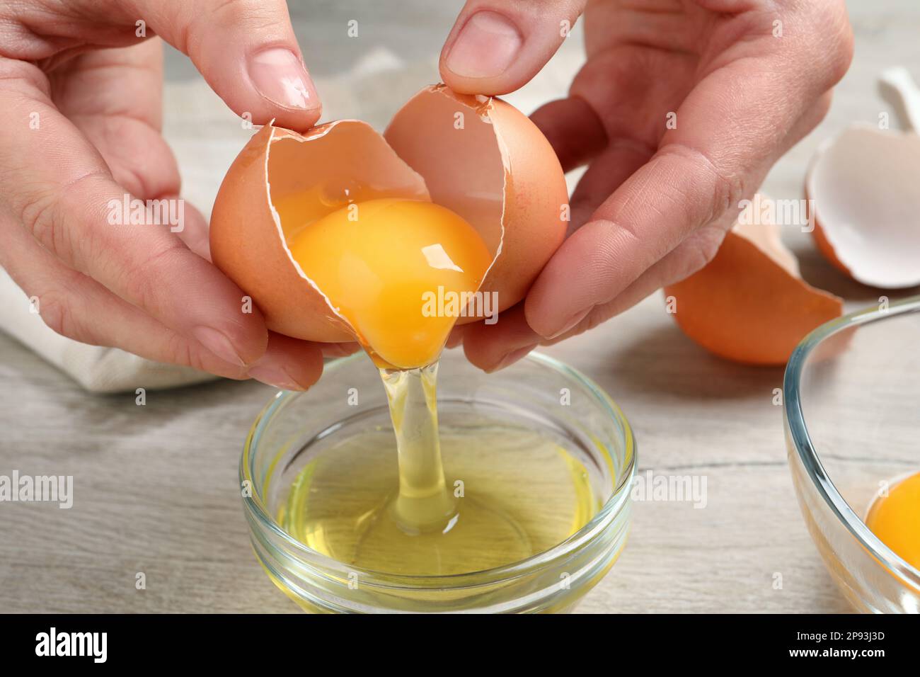 Woman separating egg yolk from white over glass bowl at wooden table, closeup Stock Photo - Alamy