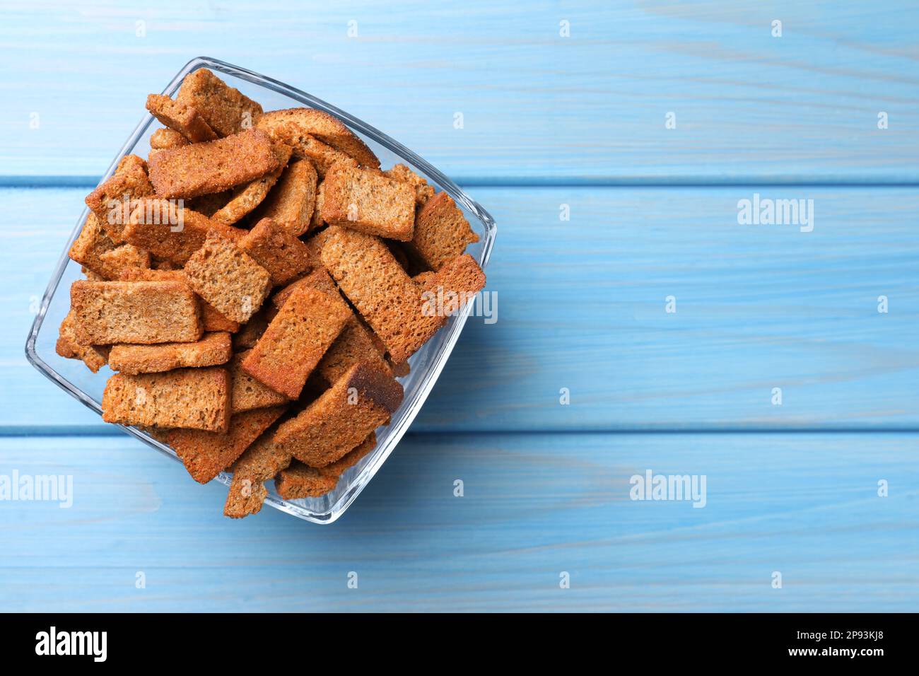 Crispy rye rusks in bowl on light blue wooden table, top view. Space ...