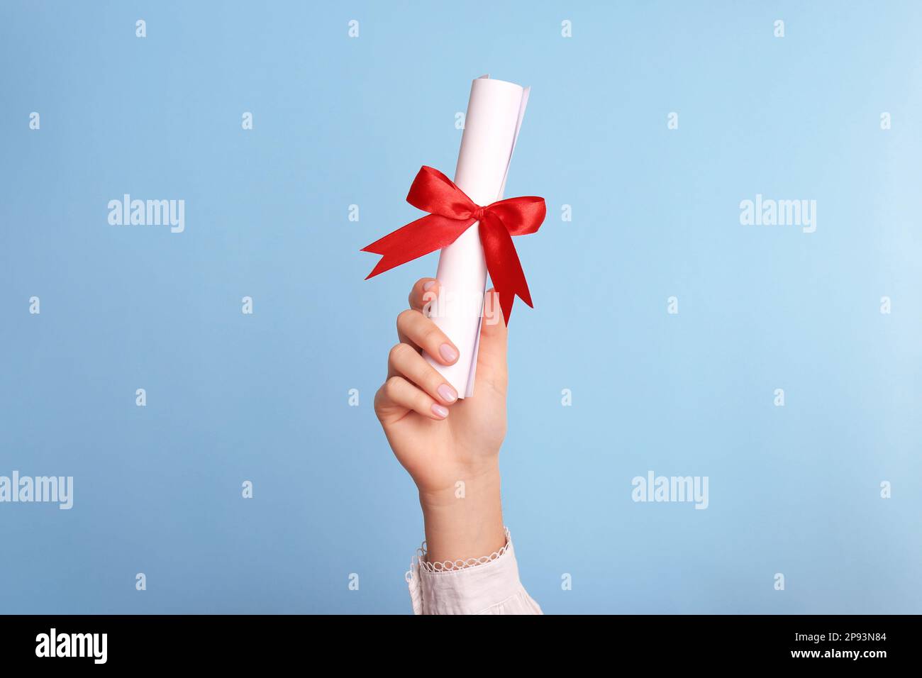 Student holding rolled diploma with red ribbon on light blue background ...