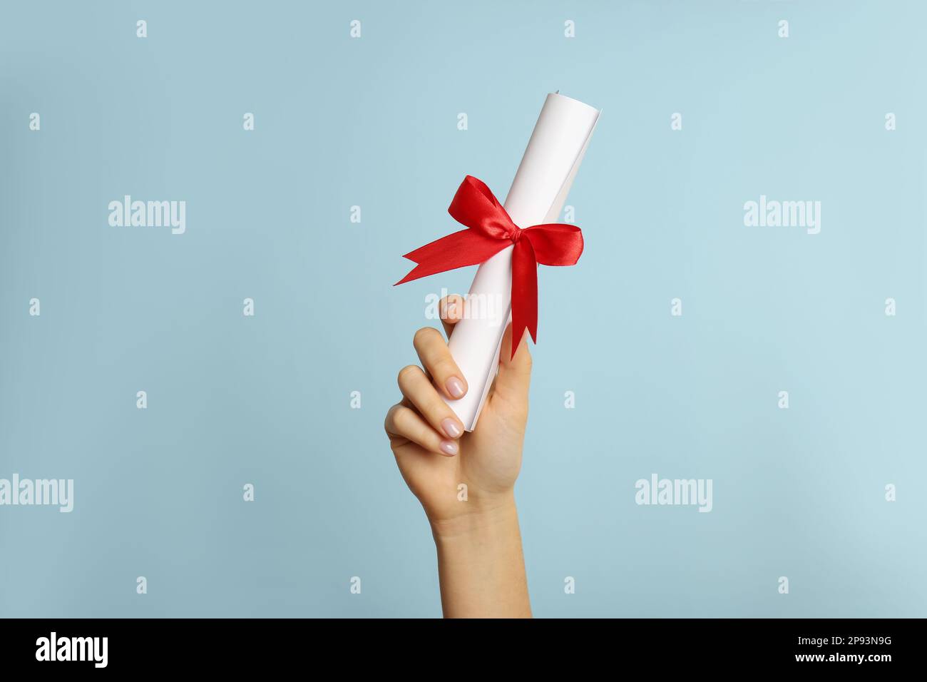 Student holding rolled diploma with red ribbon on light blue background ...