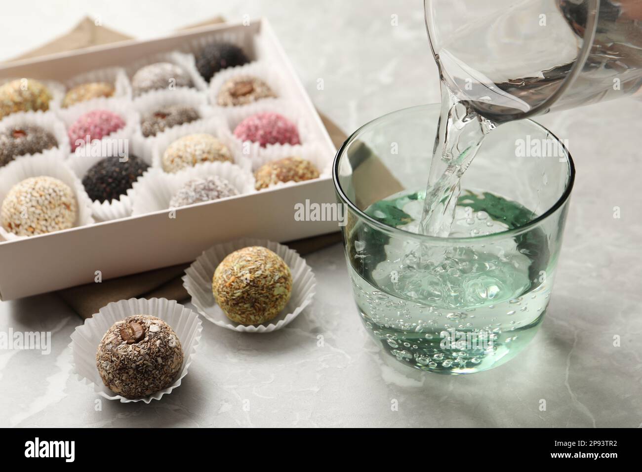 Pouring water into glass and delicious vegan candy balls at light grey ...