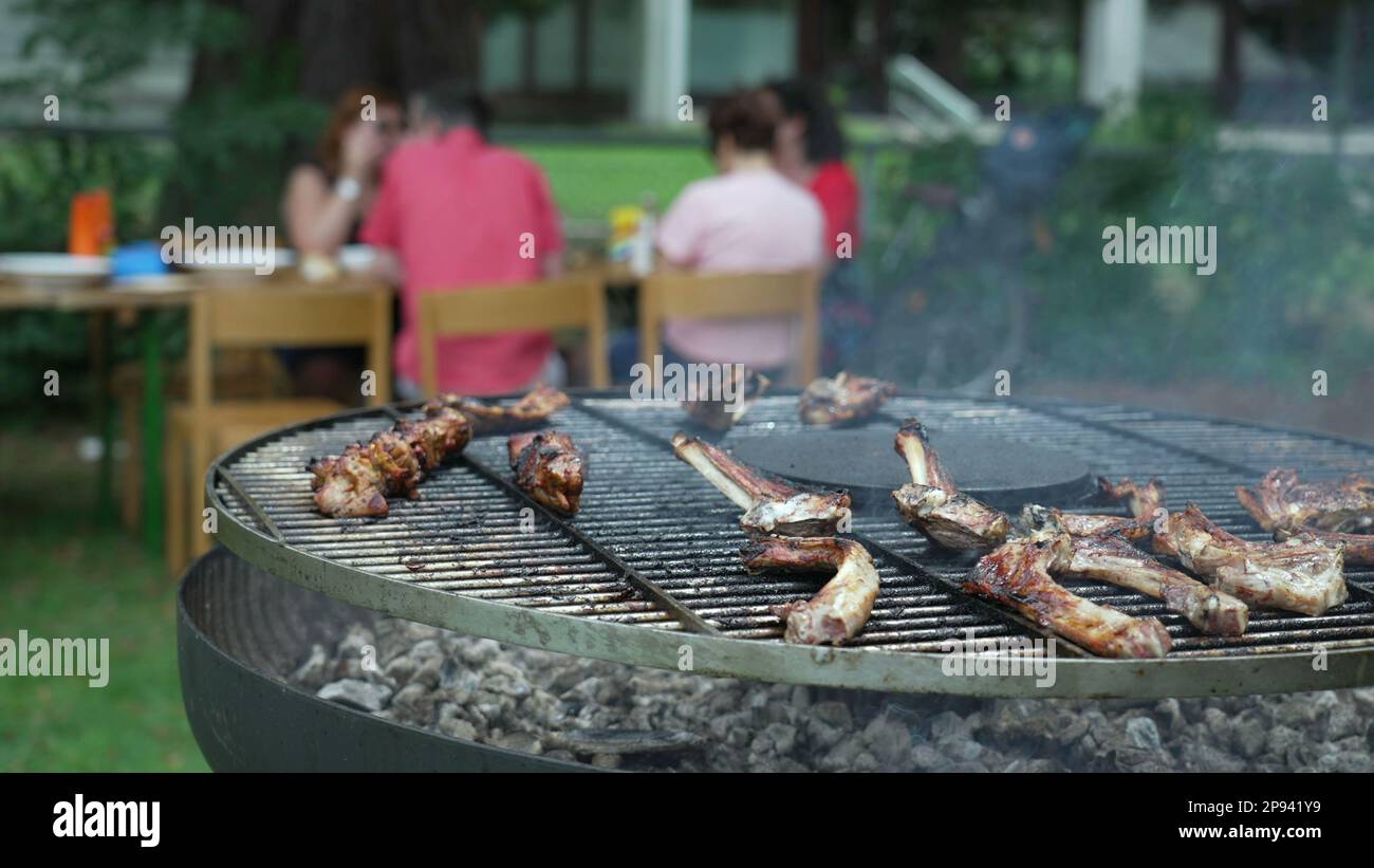 Food cooking on barbecue grill with people in background. Friends and ...