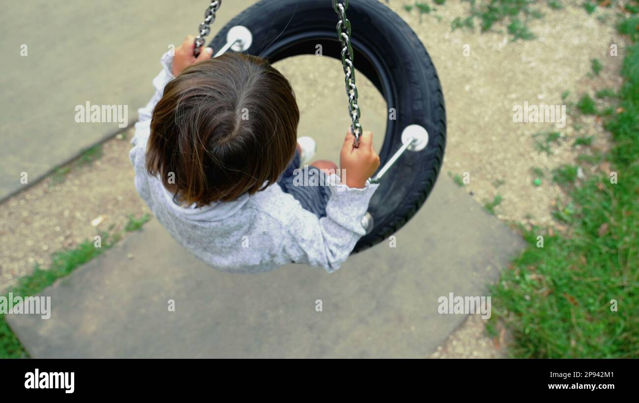 Child seated on tire swing spinning at playground park daydreaming. Top ...
