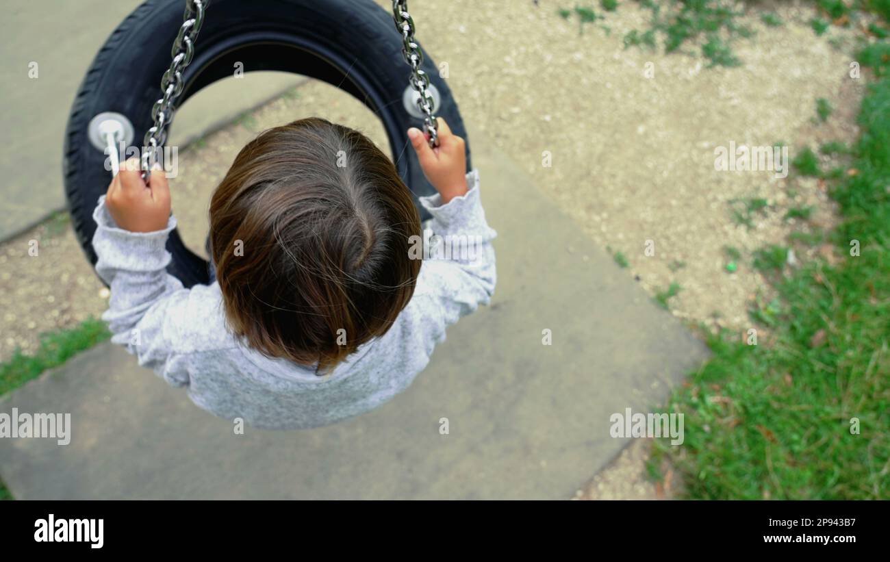 Child seated on tire swing spinning at playground park daydreaming. Top ...