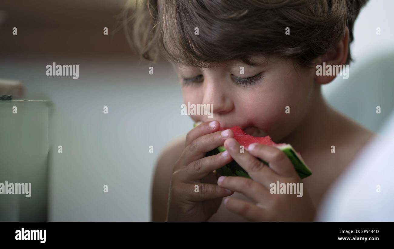 Candid child taking a bite of red watermelon fruit. One small boy ...
