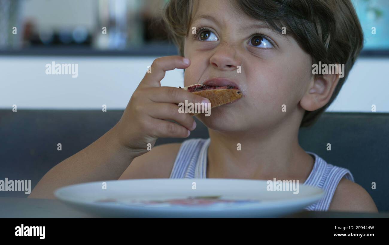 Child eating bread with jelly in morning breafast table. Candid small ...