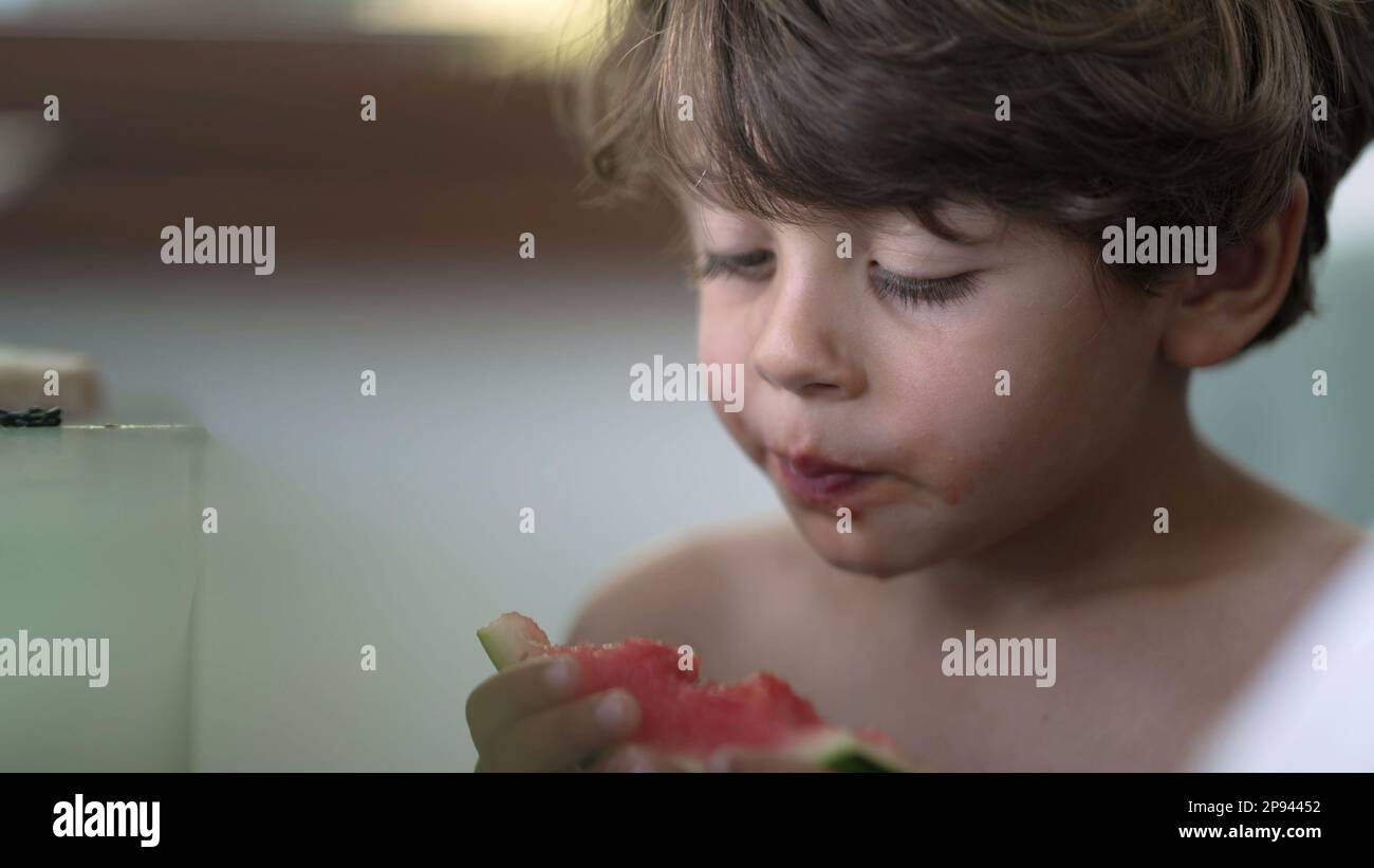 Candid child taking a bite of red watermelon fruit. One small boy ...