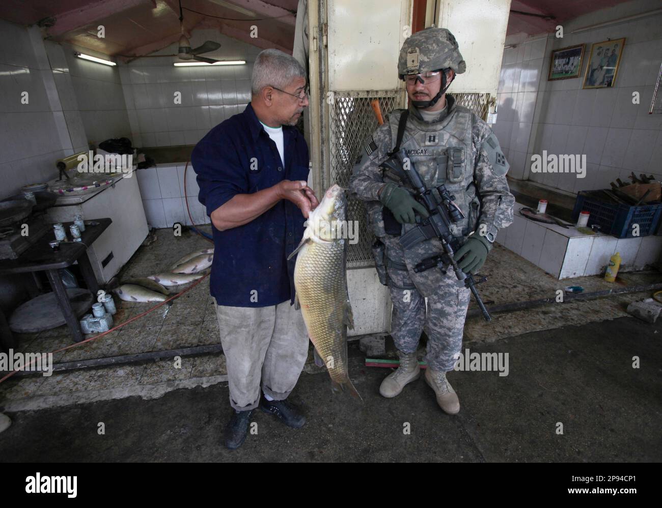 A shopkeeper shows fish to a U.S. soldier as a fish market reopens ...