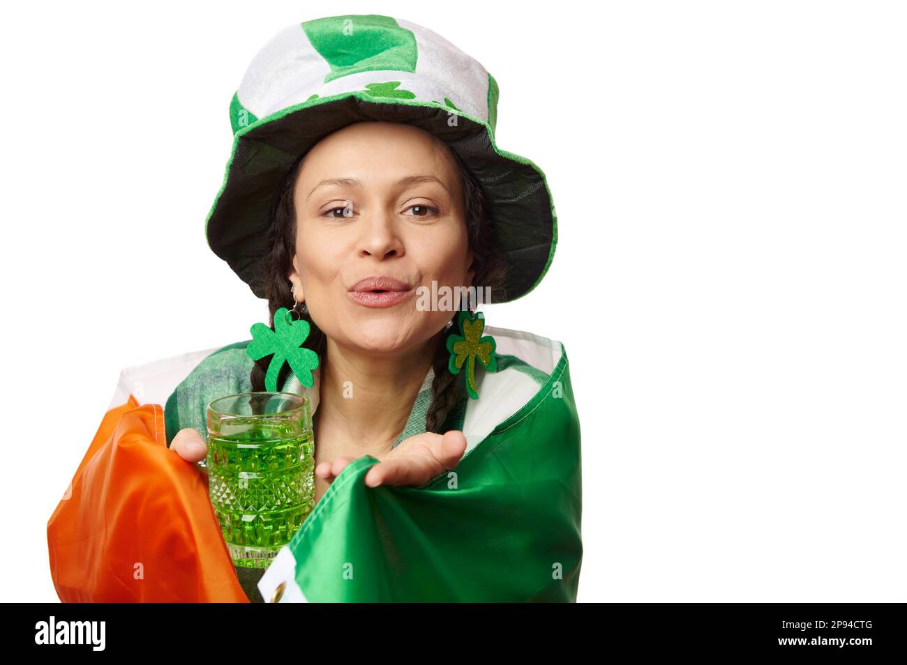 Pretty woman in Leprechaun hat, holding mug with Irish green beer, blowing air kiss, wrapped in ...