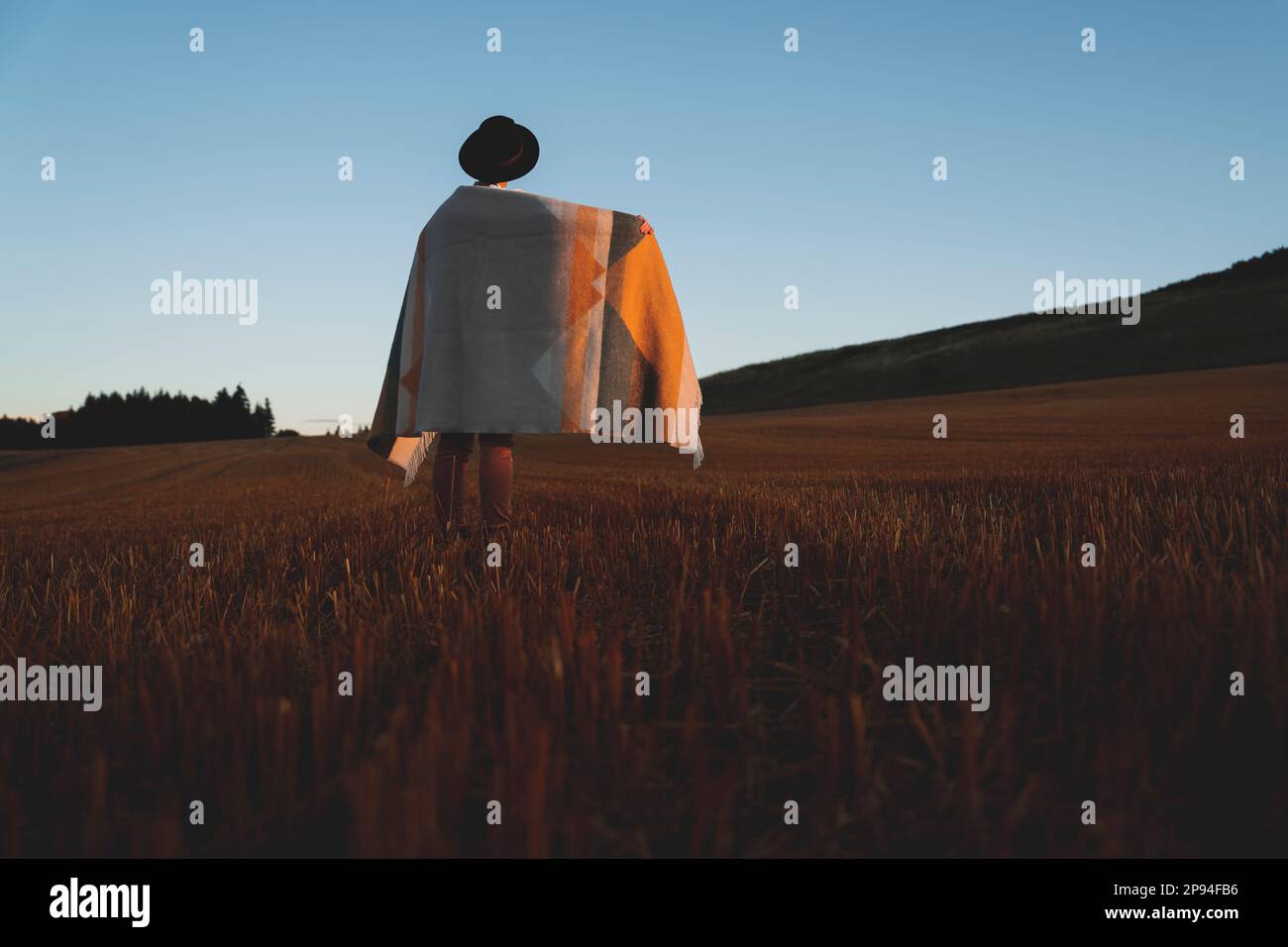 Woman with hat and wool blanket in stubble field, sunset Stock Photo ...