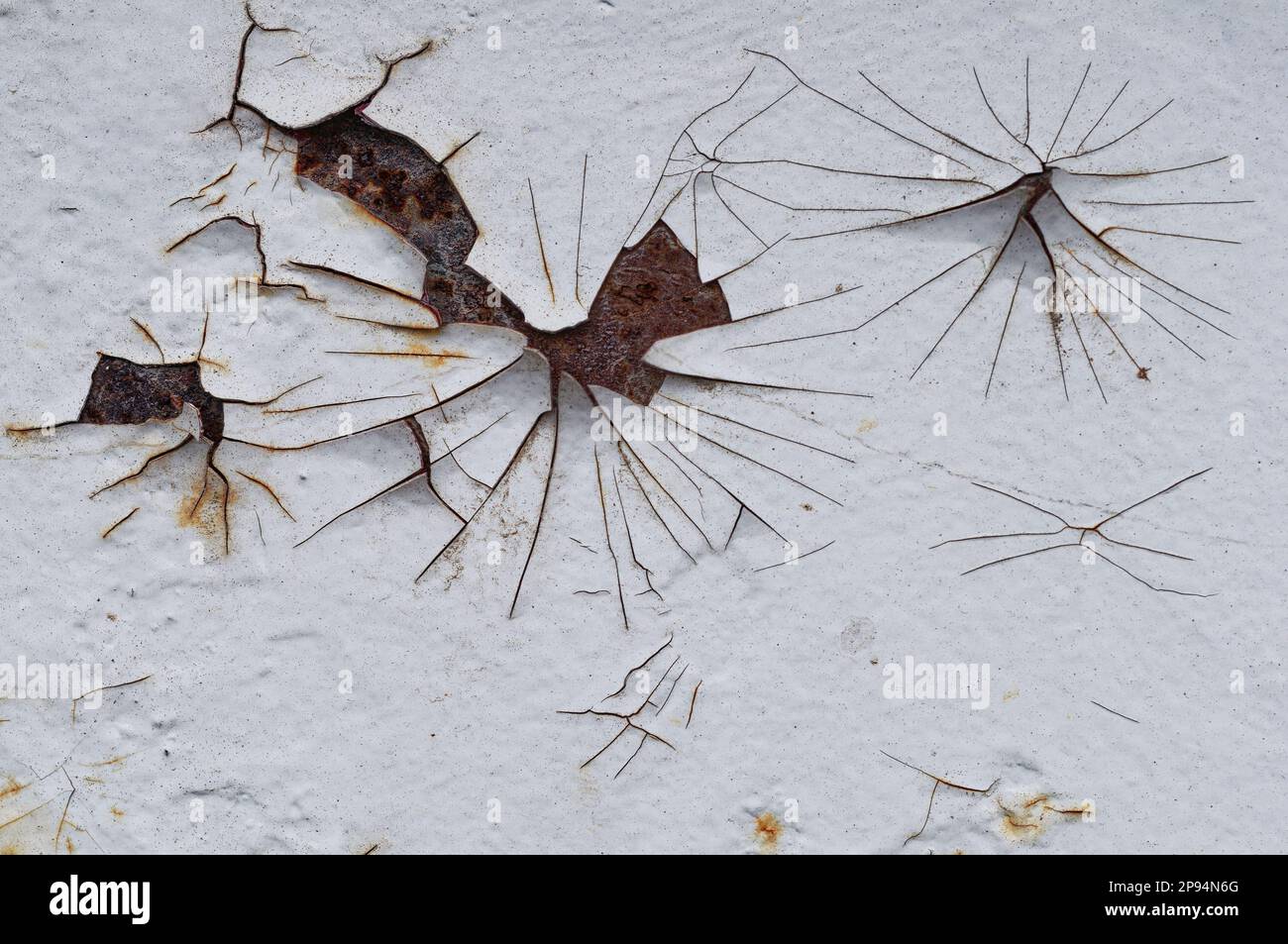 A close-up view of a white wall with chipped paint and rust, revealing ...