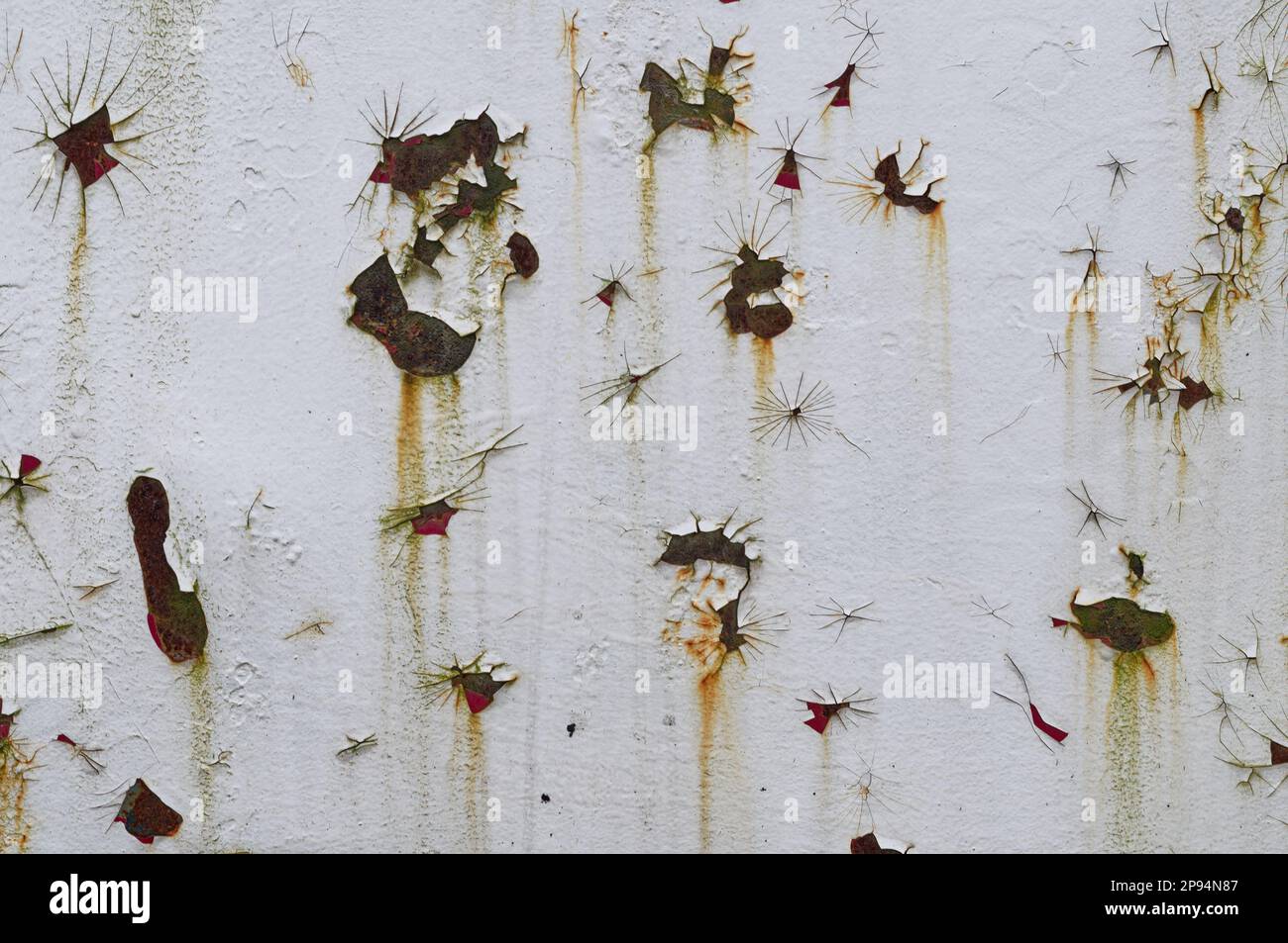 A close-up view of a white wall with chipped paint and rust, revealing ...