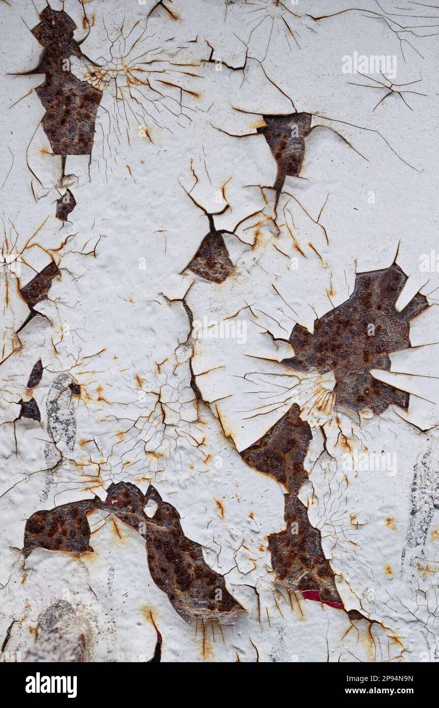 A close-up view of a white wall with chipped paint and rust, revealing ...