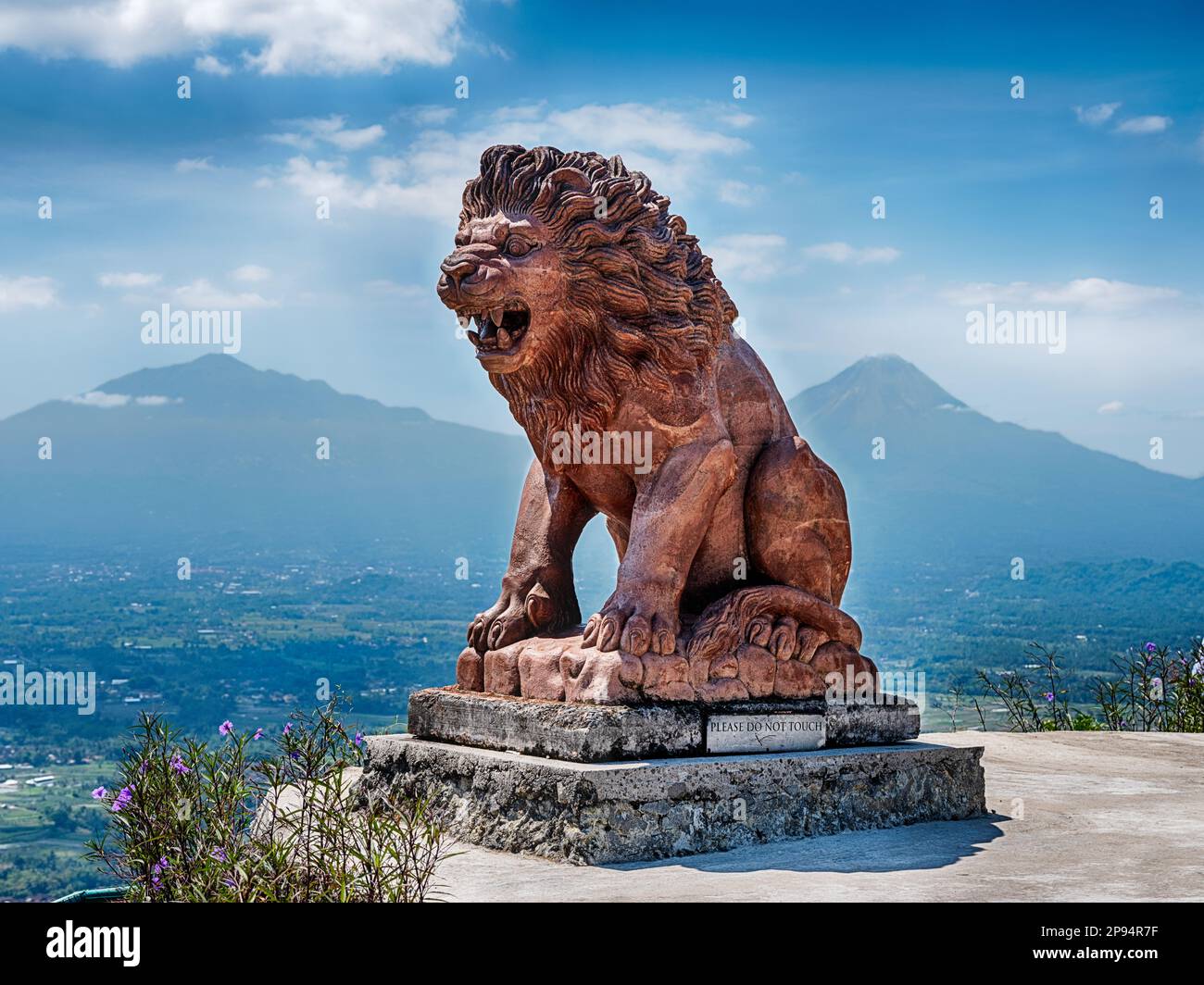 Statue of a lion looking out over the landscape of Java with two ...