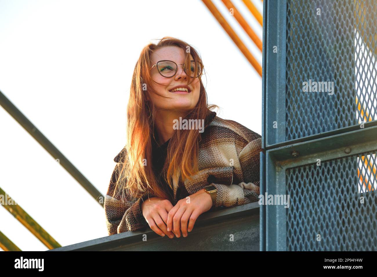 Young woman with reddish hair and glasses in plaid shirt jacket leans ...