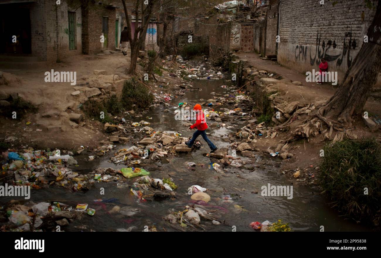 A Pakistani boy crosses a polluted river in a shanty town in Islamabad ...