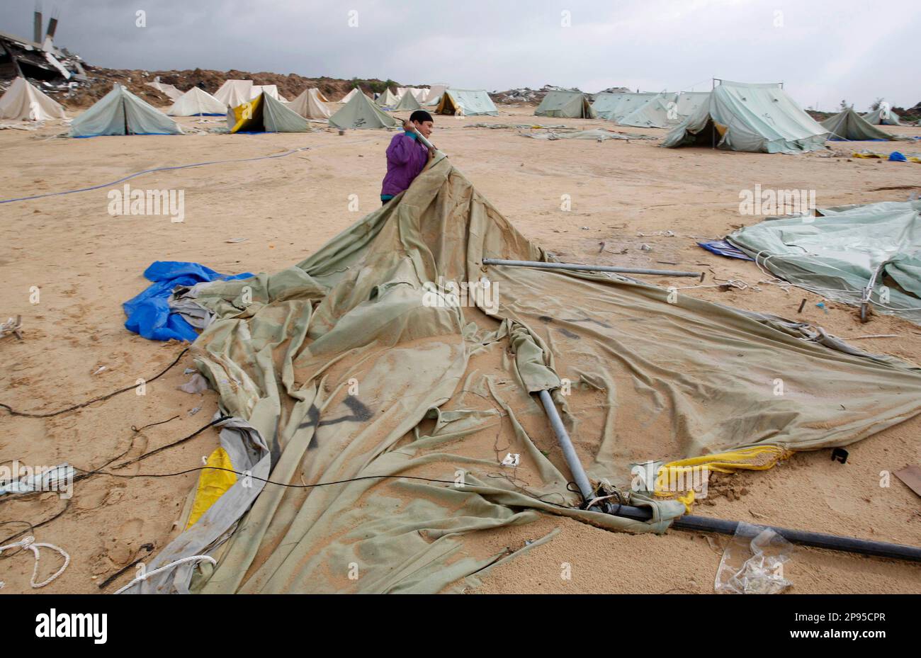 A Palestinian youth picks up a rod of a collapsed tent that housed ...
