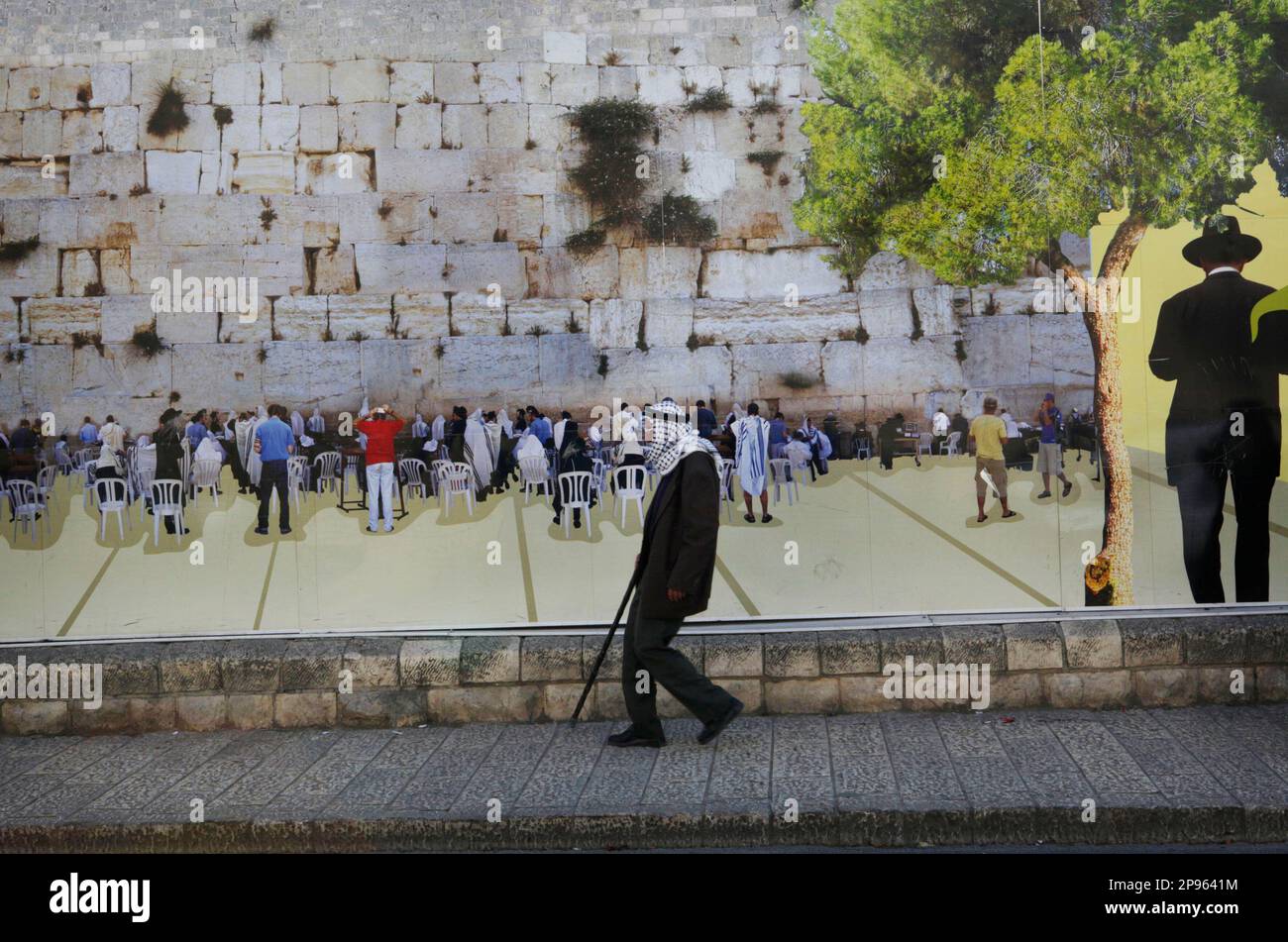 A Palestinian walks downhill as he passes a painting of the Western ...